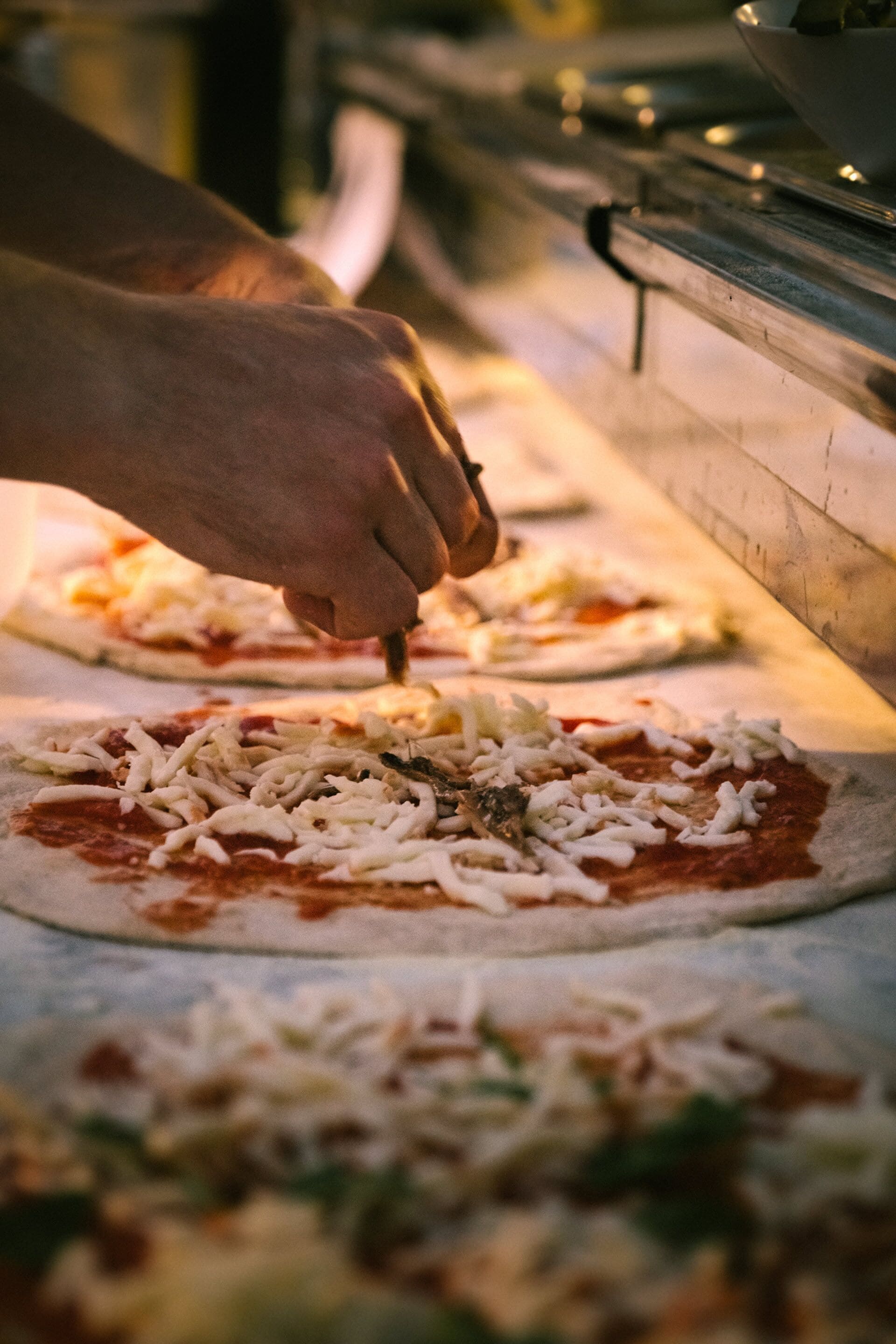Uma pessoa preparando pizzas com queijo e molho de tomate em uma superfície plana.