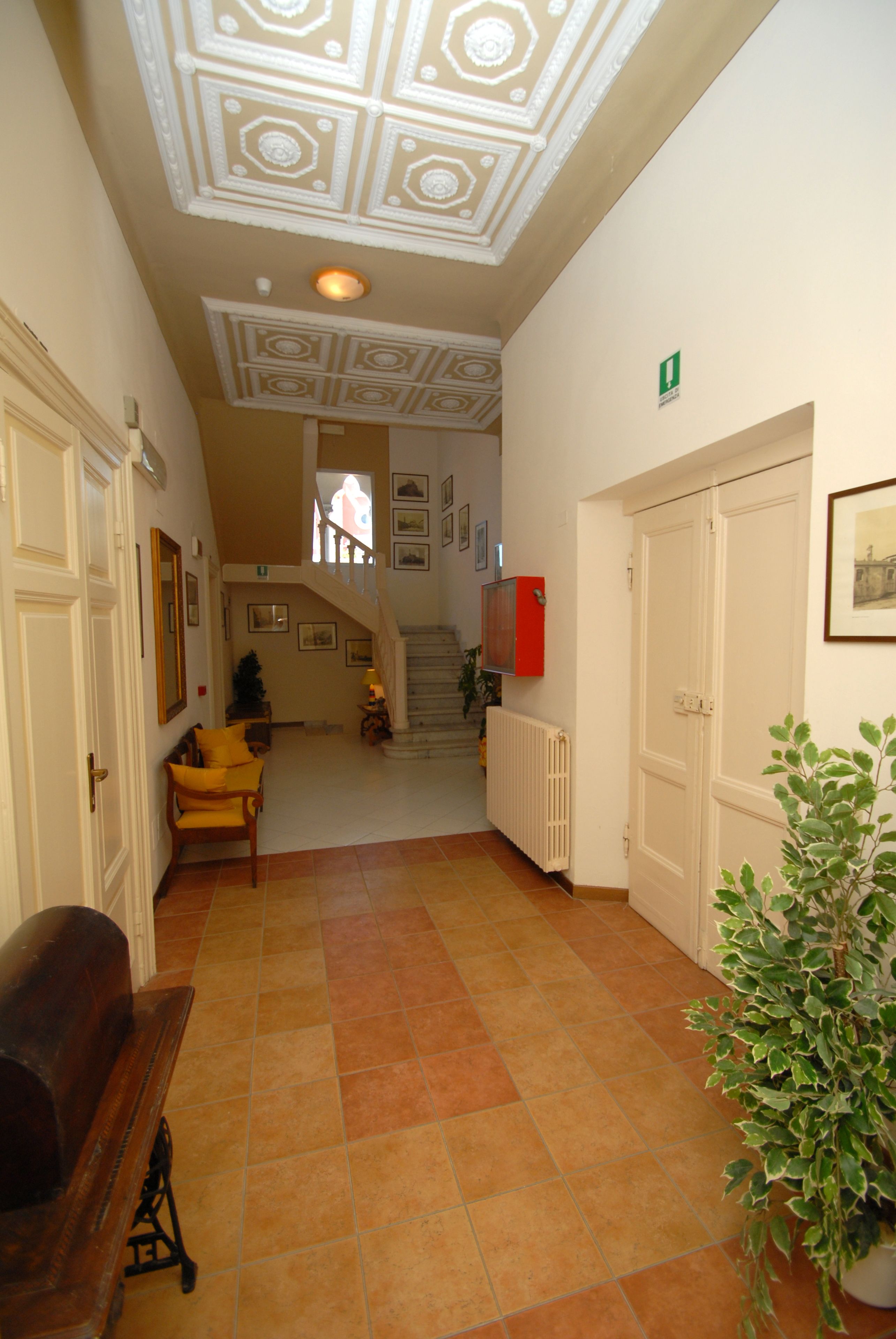 Um corredor com piso de azulejos, um piano, uma escadaria e uma planta.