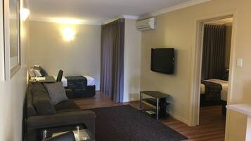 Quarto de hotel com sofá, televisão pequena, ar condicionado, escrivaninha e cama com cortinas.