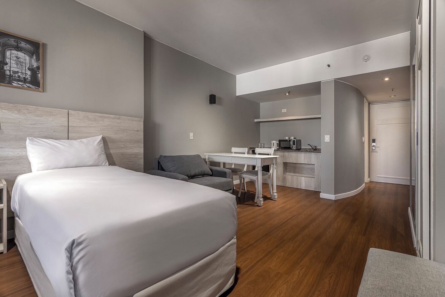 Quarto de hotel moderno com cama grande, área de refeições e cozinha compacta.