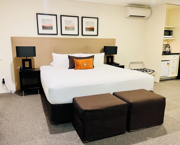 Quarto de hotel com uma cama grande, duas mesas de cabeceira com luminárias, uma TV de tela plana, um minibar e uma cozinha compacta.