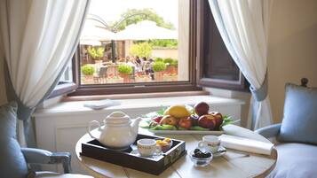 Bandeja de café da manhã com bule, xícara e frutas sobre uma mesa próxima a uma janela com cortinas.