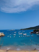 Vista costeira com barcos, uma praia de areia e terreno rochoso.
