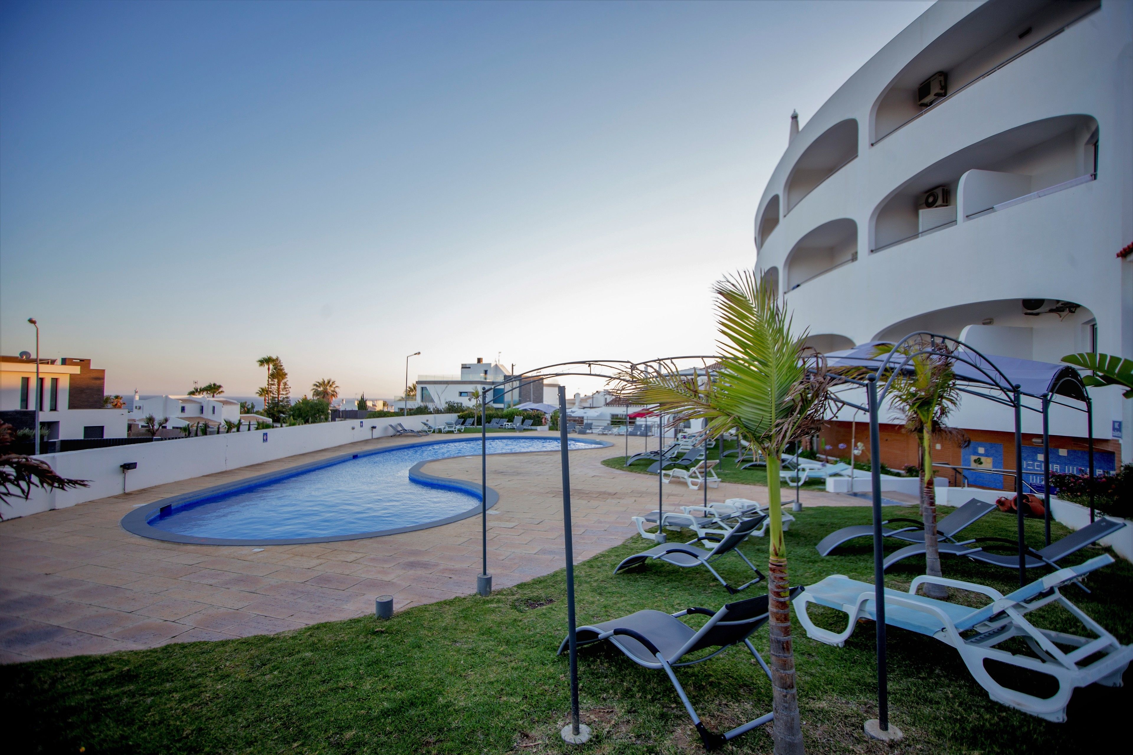Piscina com espreguiçadeiras e um edifício com varandas.