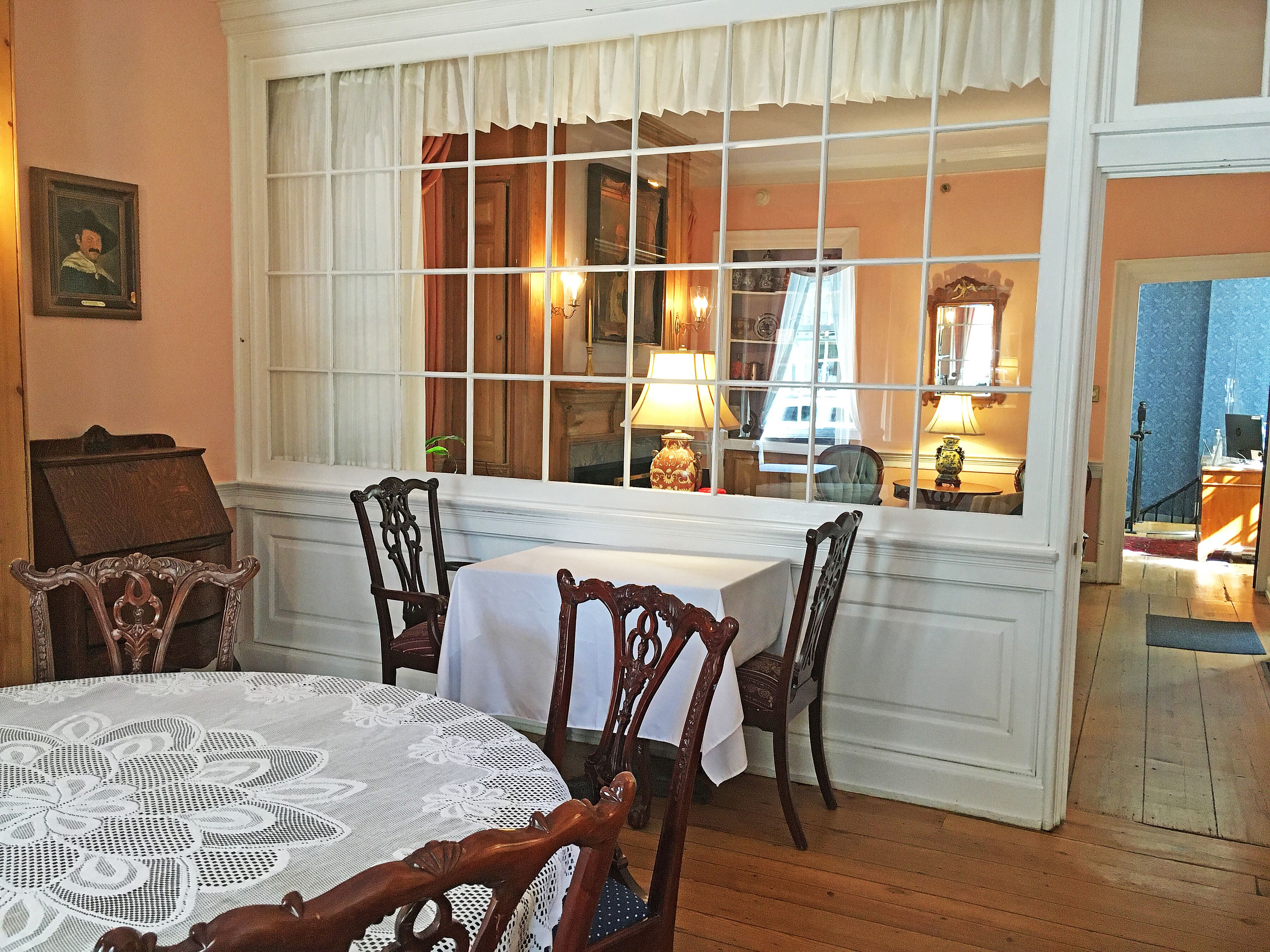Uma sala de jantar com mesa e cadeiras, uma janela com cortinas e um quadro na parede.