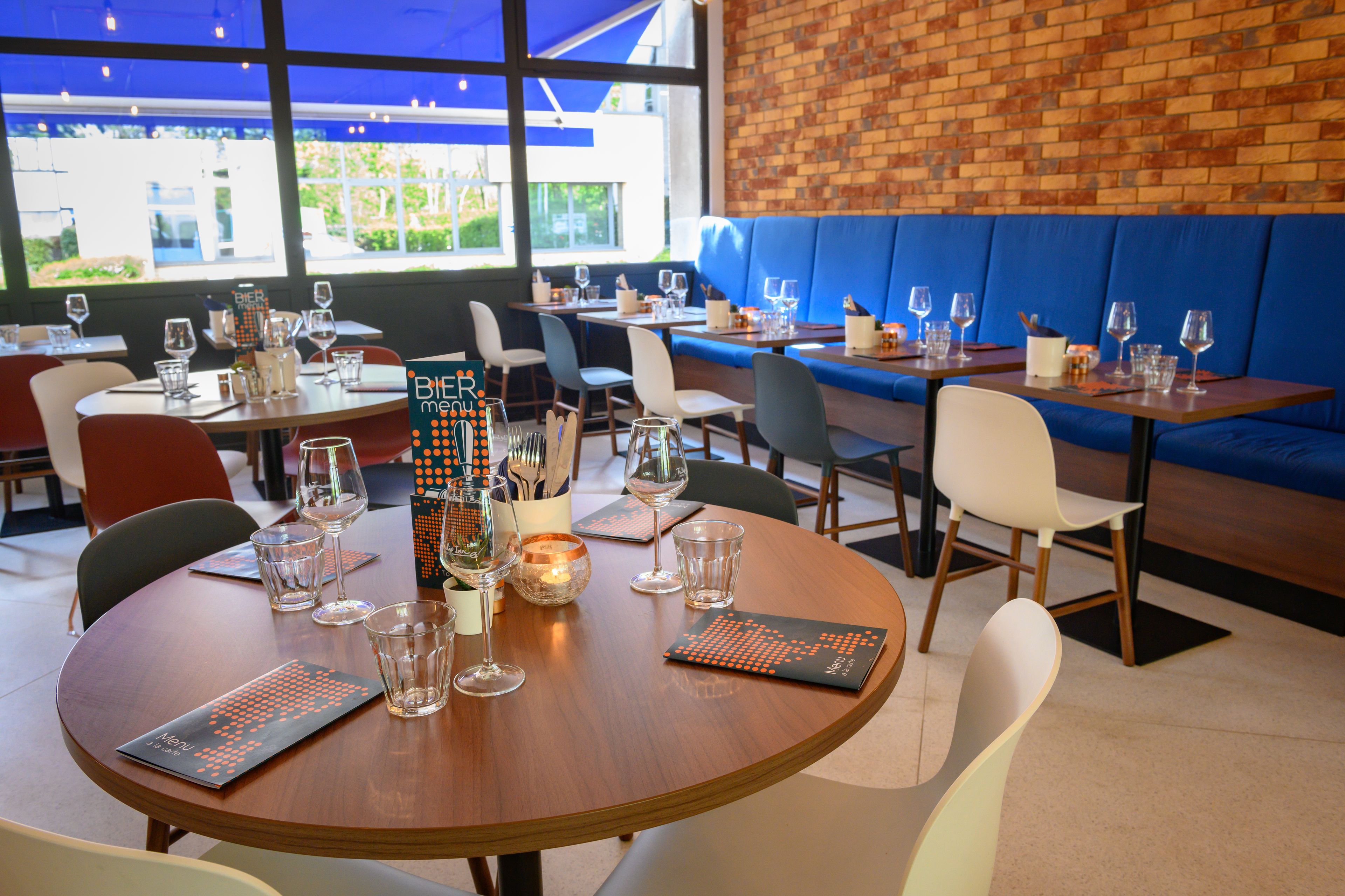 Um restaurante com mesas redondas, assentos acolchoados em azul e uma parede de tijolos.