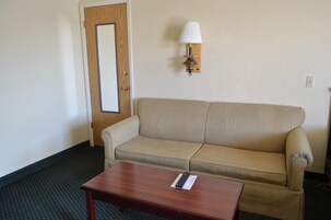 Um quarto com um sofá bege, uma mesa de madeira, uma luminária na parede e uma porta.