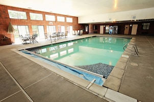 Piscina interna com paredes azulejadas, um deck de piscina azul e uma área de estar com mesas e cadeiras.