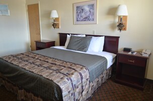 Quarto de hotel com uma cama grande, duas mesas de cabeceira, um criado-mudo, uma luminária e um quadro na parede.