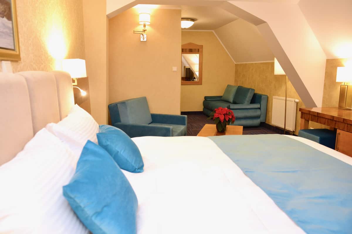 Quarto de hotel com uma cama grande, duas poltronas, uma mesinha de centro com um vaso e um espelho na parede.