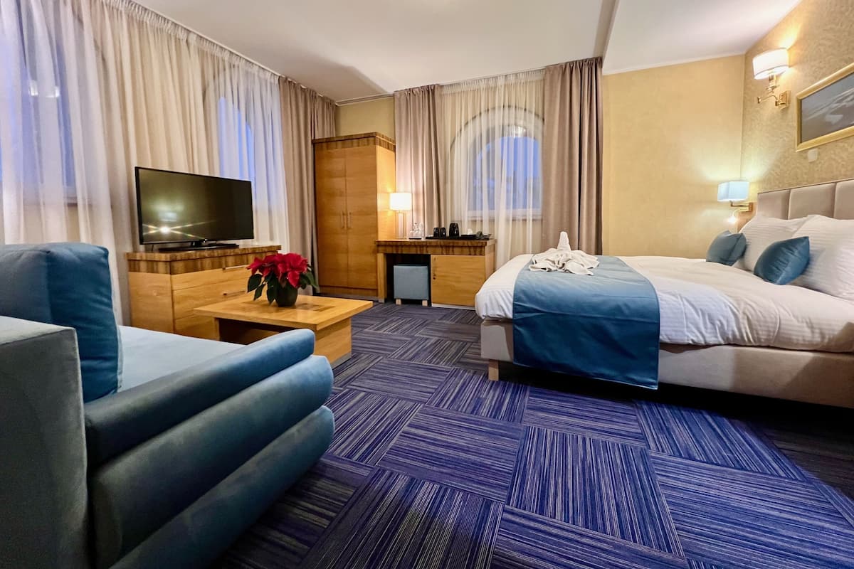 Quarto de hotel com cama, sofá, televisão, escrivaninha e janela com cortinas.