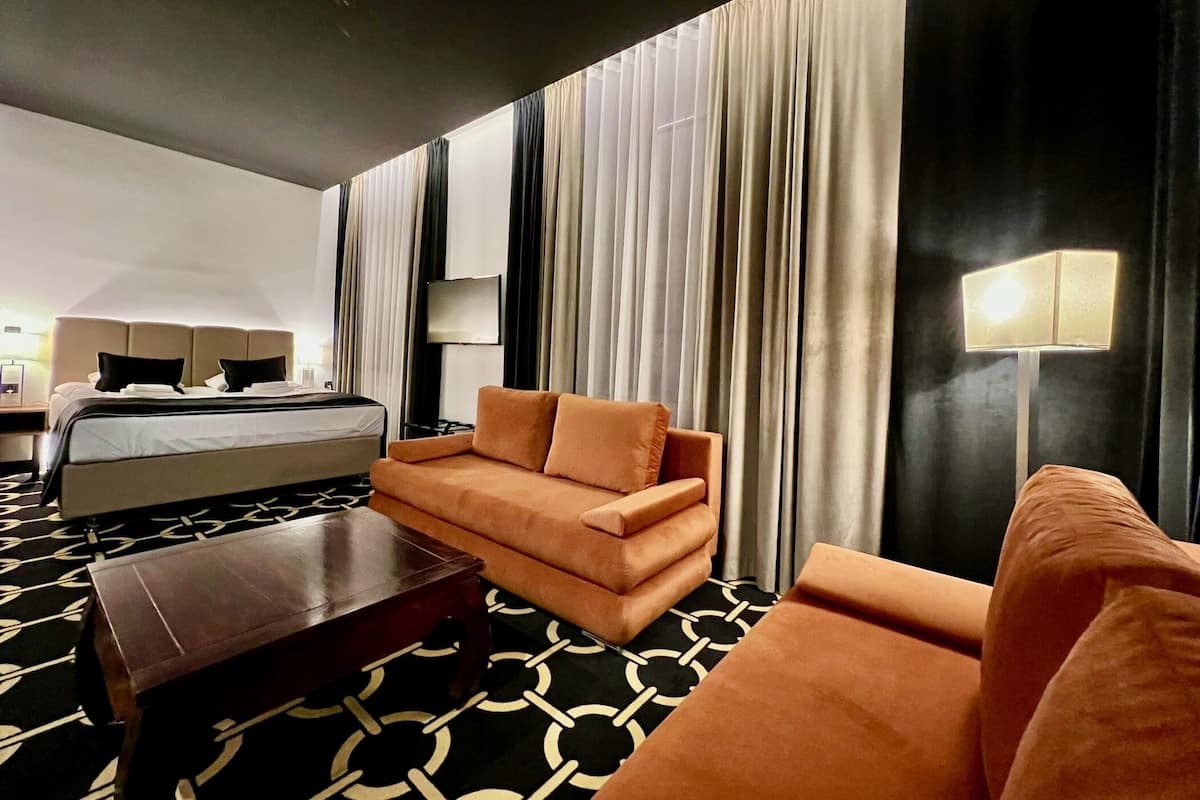 Quarto de hotel com cama, sofá, mesa de centro e luminária.