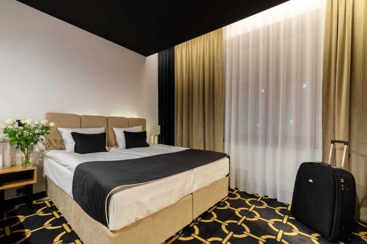 Quarto de hotel com uma cama, mesa de cabeceira, um vaso com flores e uma mala.