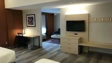 Quarto de hotel com cama, escrivaninha, cadeira, televisão e cómoda.