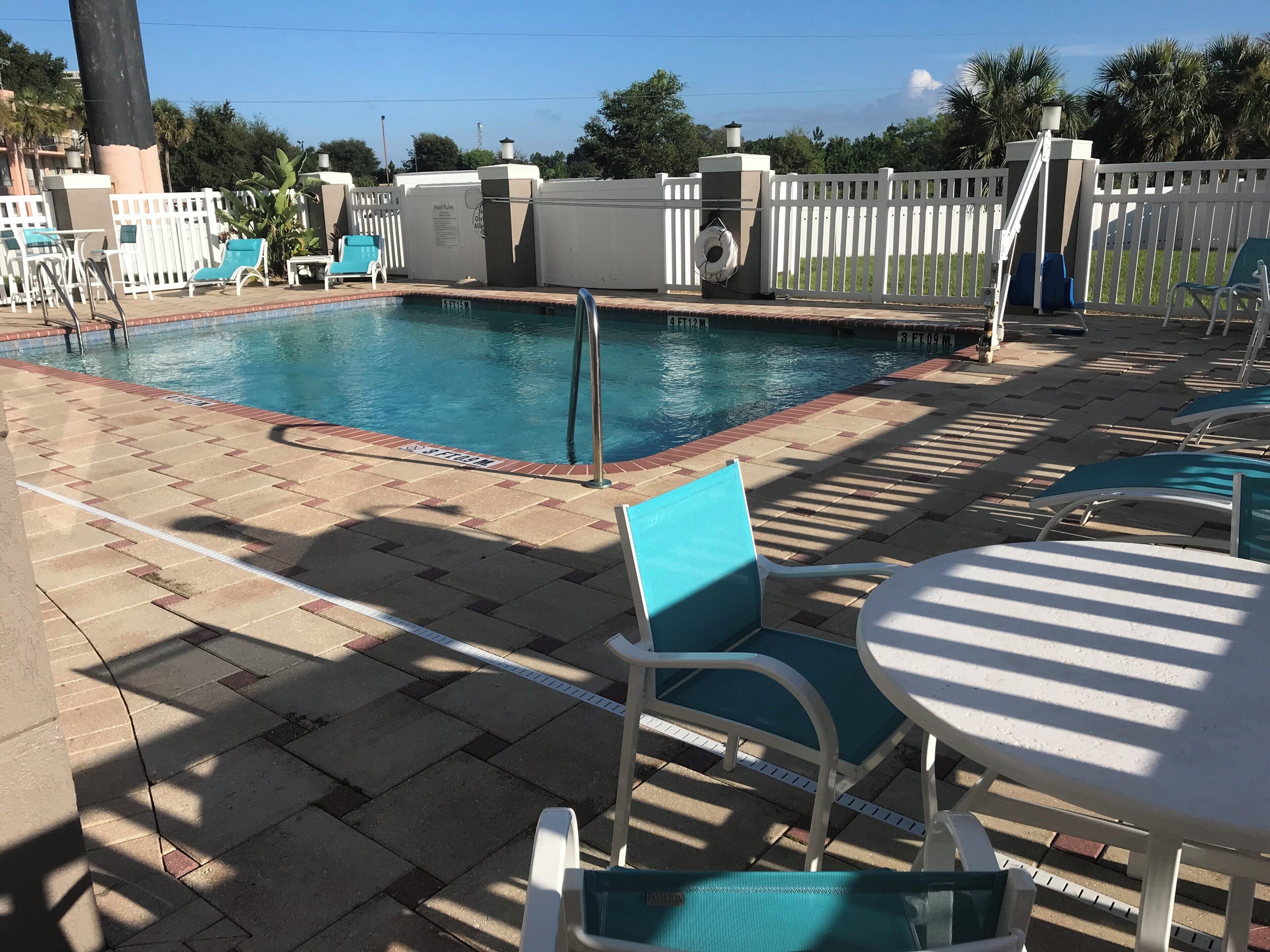 Piscina com cerca branca, cadeiras de descanso e uma mesa.
