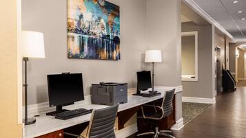 Espaço de trabalho em hotel com duas mesas, computadores e cadeiras.