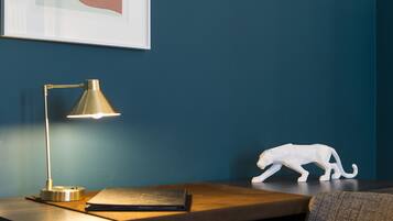 Um quarto com uma escrivaninha, luminária, escultura branca, quadro emoldurado e almofada estampada.