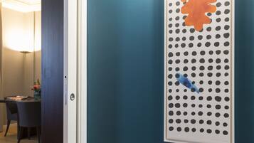 Um corredor com parede azul-esverdeada, porta branca e painel decorativo fixado na parede com padrão geométrico.