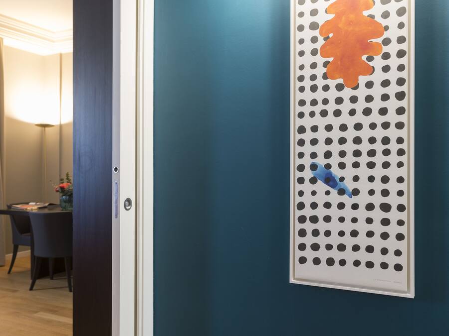 Um corredor com parede azul-esverdeada, porta branca e painel decorativo fixado na parede com padrão geométrico.