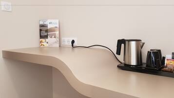 Uma área de recepção de hotel com um balcão curvo, chaleira, máquina de café e um folheto na parede.