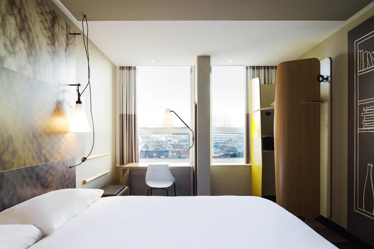 Quarto de hotel com uma cama grande, uma escrivaninha, uma cadeira e um guarda-roupa.