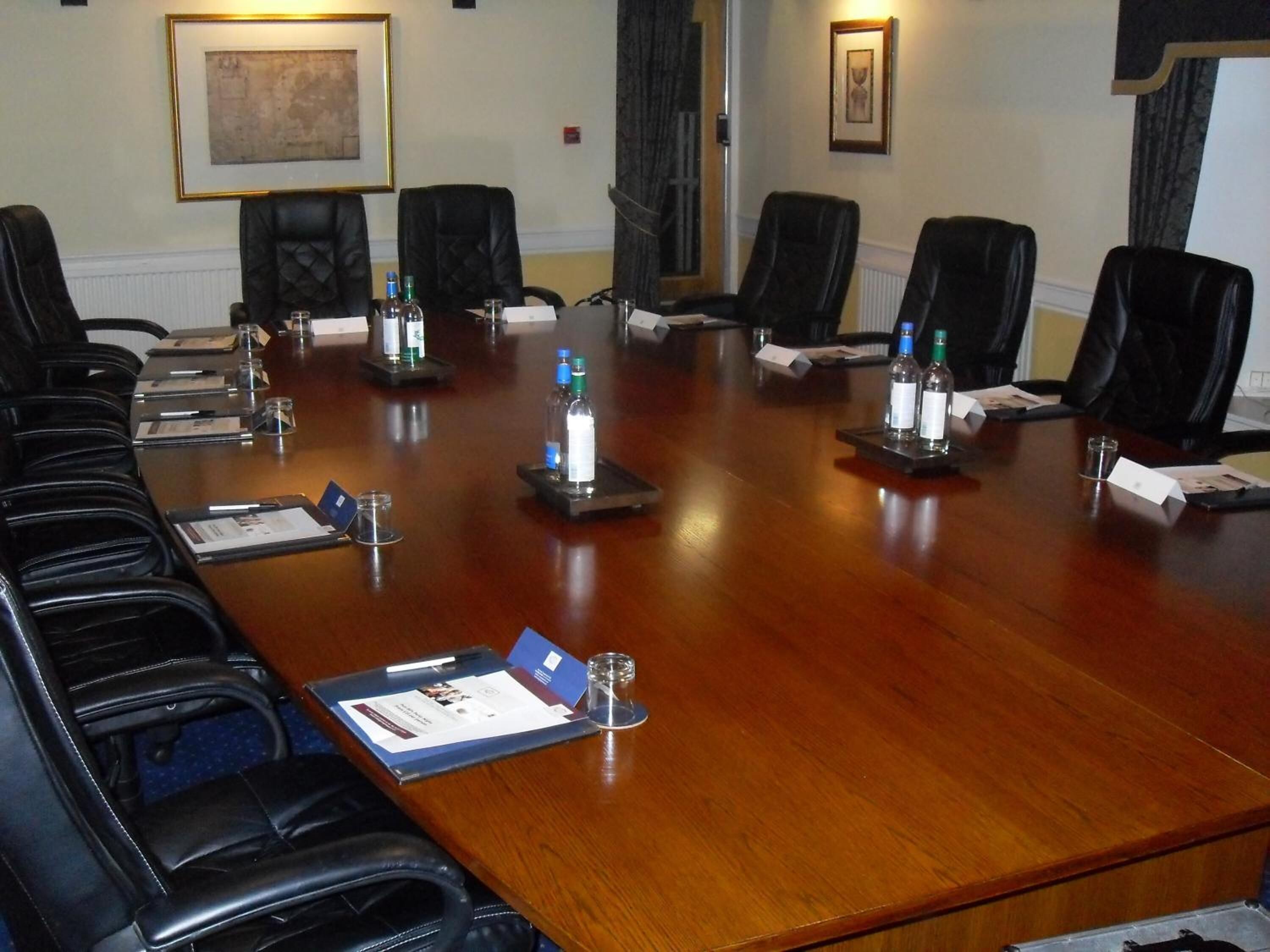 Uma sala de conferências com uma longa mesa de madeira, cadeiras de couro preto e placas de identificação.