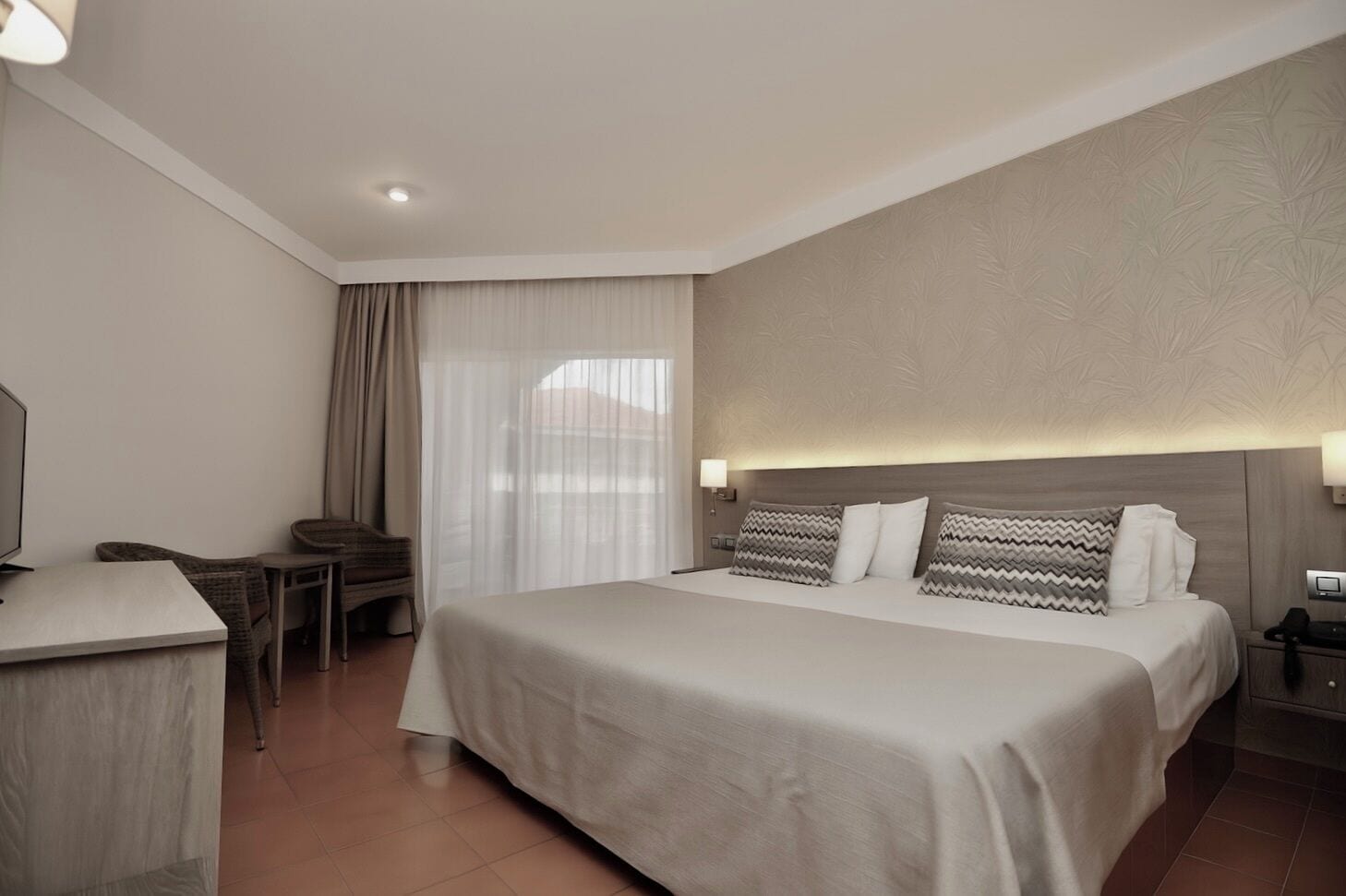 Quarto de hotel com uma cama grande, uma escrivaninha, uma cadeira e uma televisão.