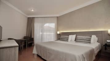 Quarto de hotel com uma cama grande, uma escrivaninha, uma cadeira e uma televisão.
