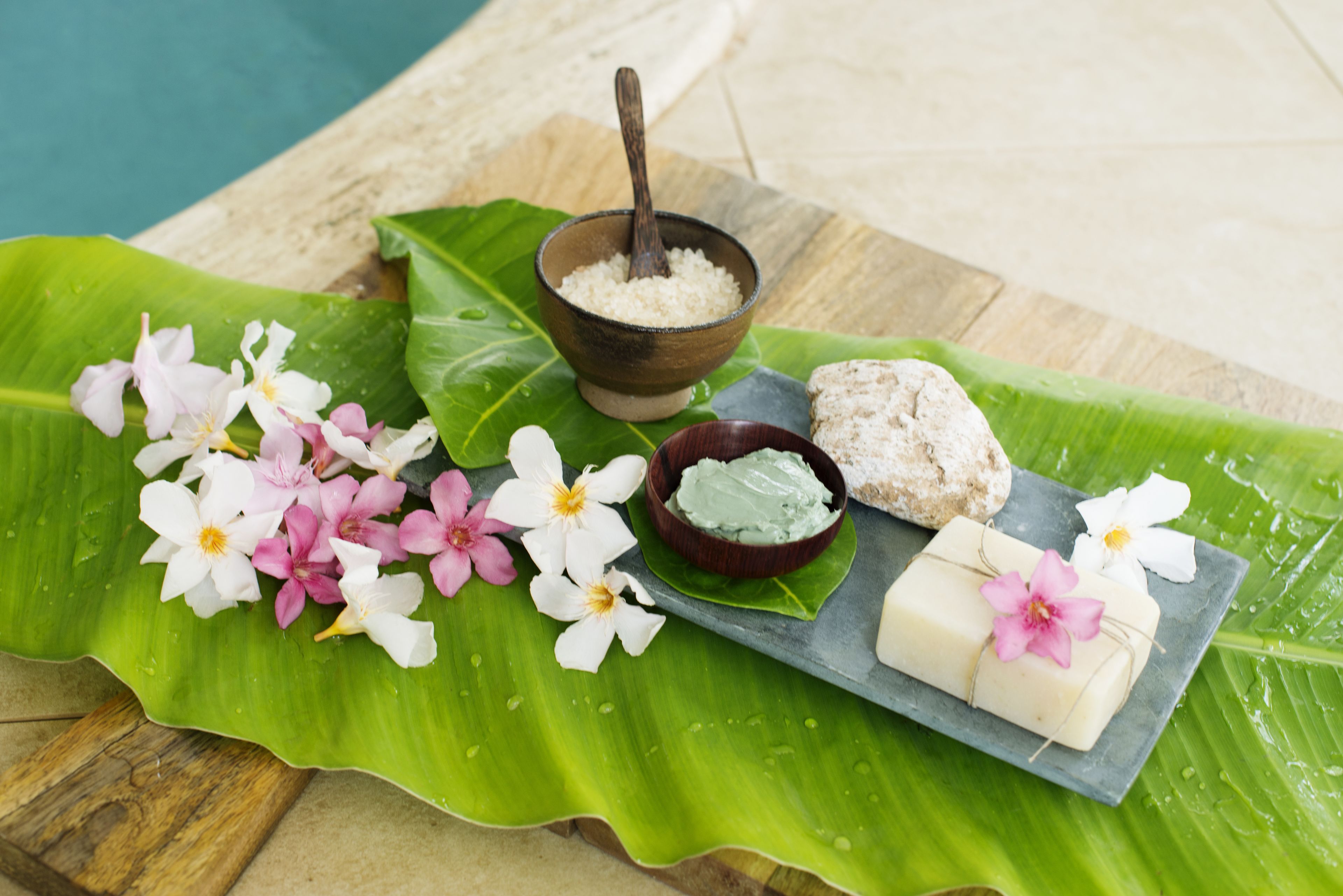 Uma bandeja com folha de bananeira, flores e uma barra de sabão sobre uma superfície de madeira.