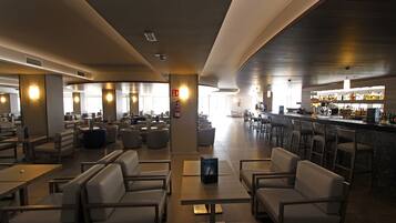Um amplo hall de hotel com várias áreas de estar, um bar com uma variedade de garrafas e um extintor de incêndio fixado na parede.