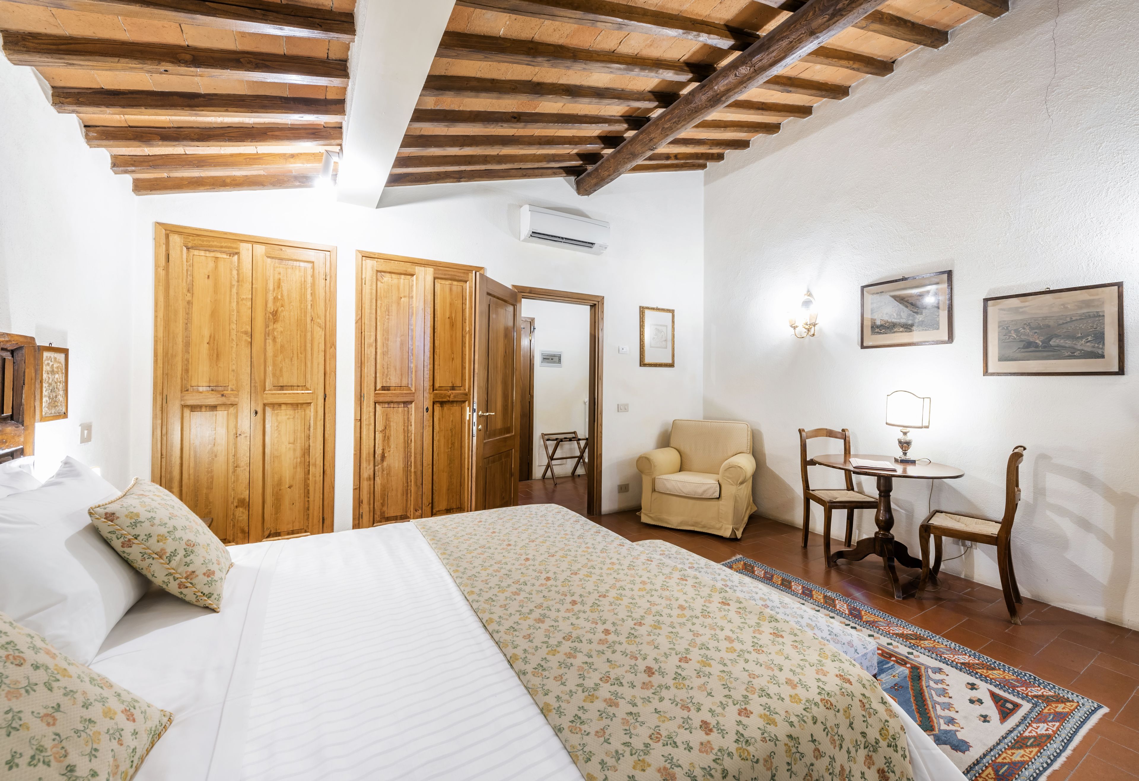Quarto com cama grande, guarda-roupa de madeira, uma cadeira, uma mesinha e uma lâmpada.