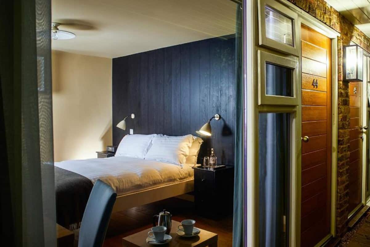 Quarto de hotel com uma cama, mesas de cabeceira, uma luminária e uma pequena mesa com xícara e pires.