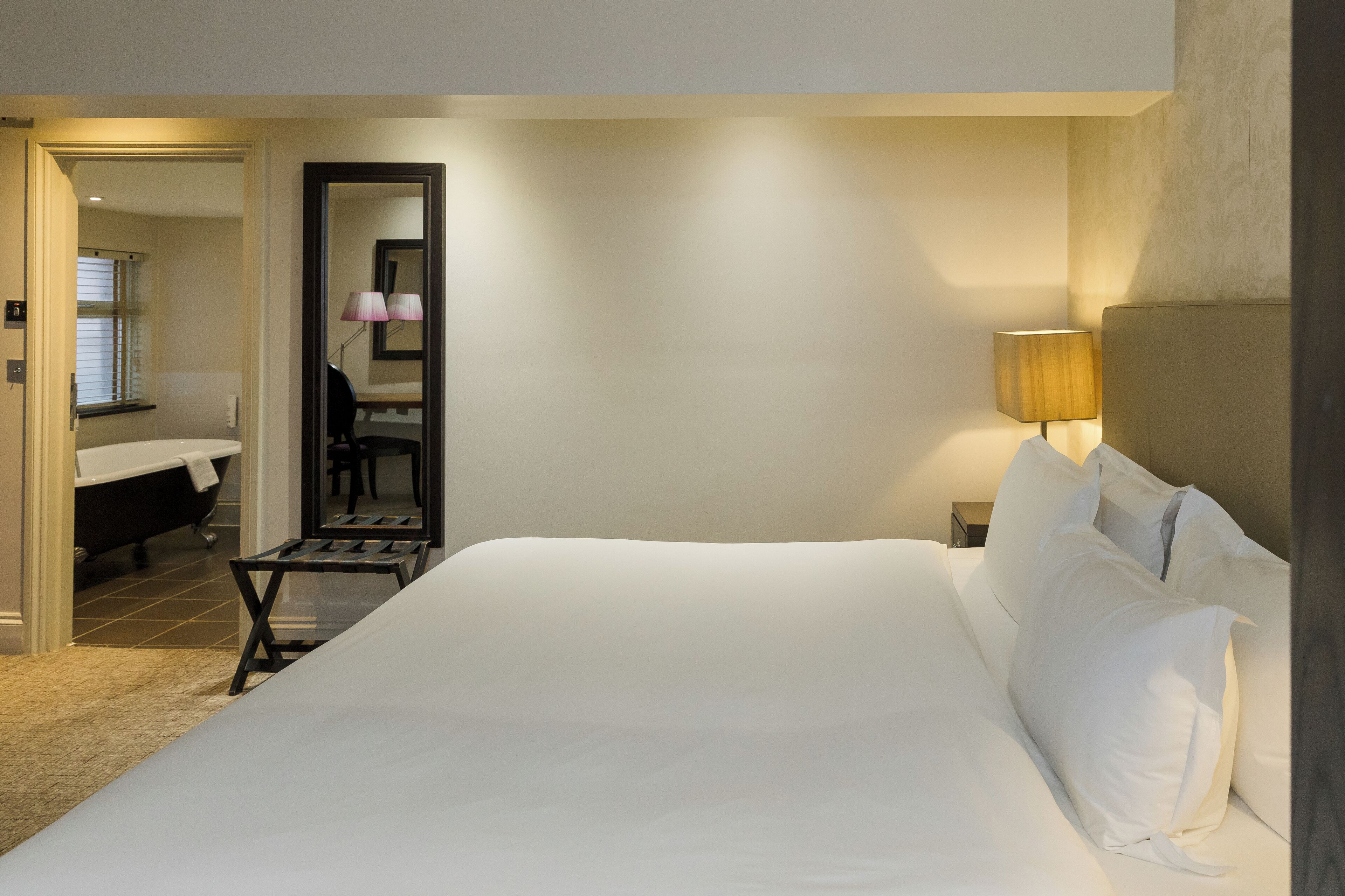 Quarto de hotel com uma cama grande, uma escrivaninha com cadeira, casa de banho com banheira e um espelho.