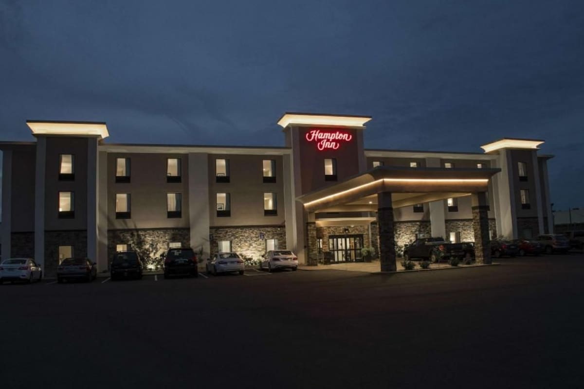 Um hotel Hampton Inn com design moderno, vários andares e uma entrada bem iluminada.