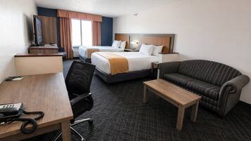 Quarto de hotel com duas camas, uma escrivaninha com telefone, uma cadeira, um sofá e uma televisão.