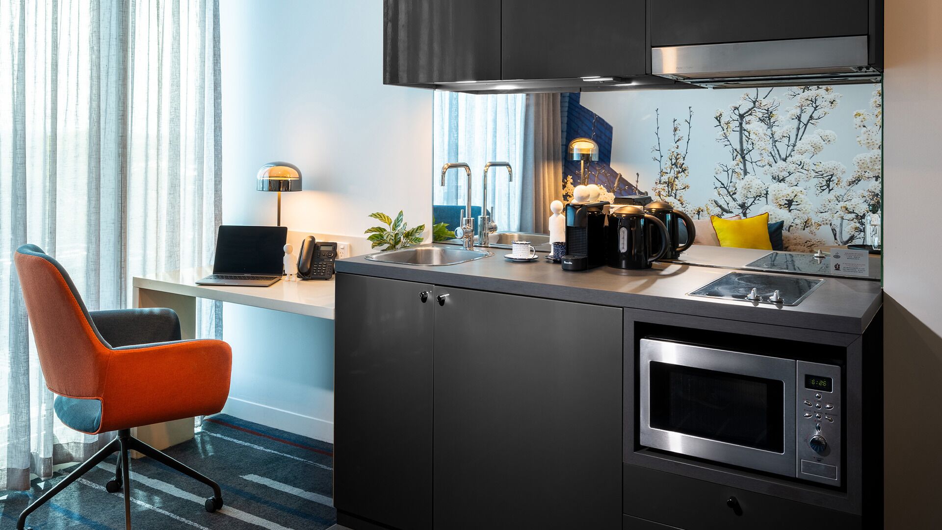 Quarto de hotel compacto com cozinha compacta, uma escrivaninha com um laptop, uma cadeira e um micro-ondas.