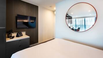 Quarto moderno com cama grande, televisão fixada na parede, mesa de cabeceira com bolsa e espelho redondo.