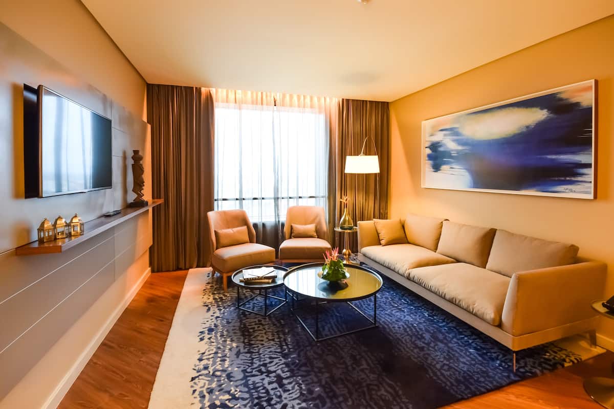 Uma sala de estar moderna com um sofá, duas poltronas, uma mesa de centro e uma televisão na parede.