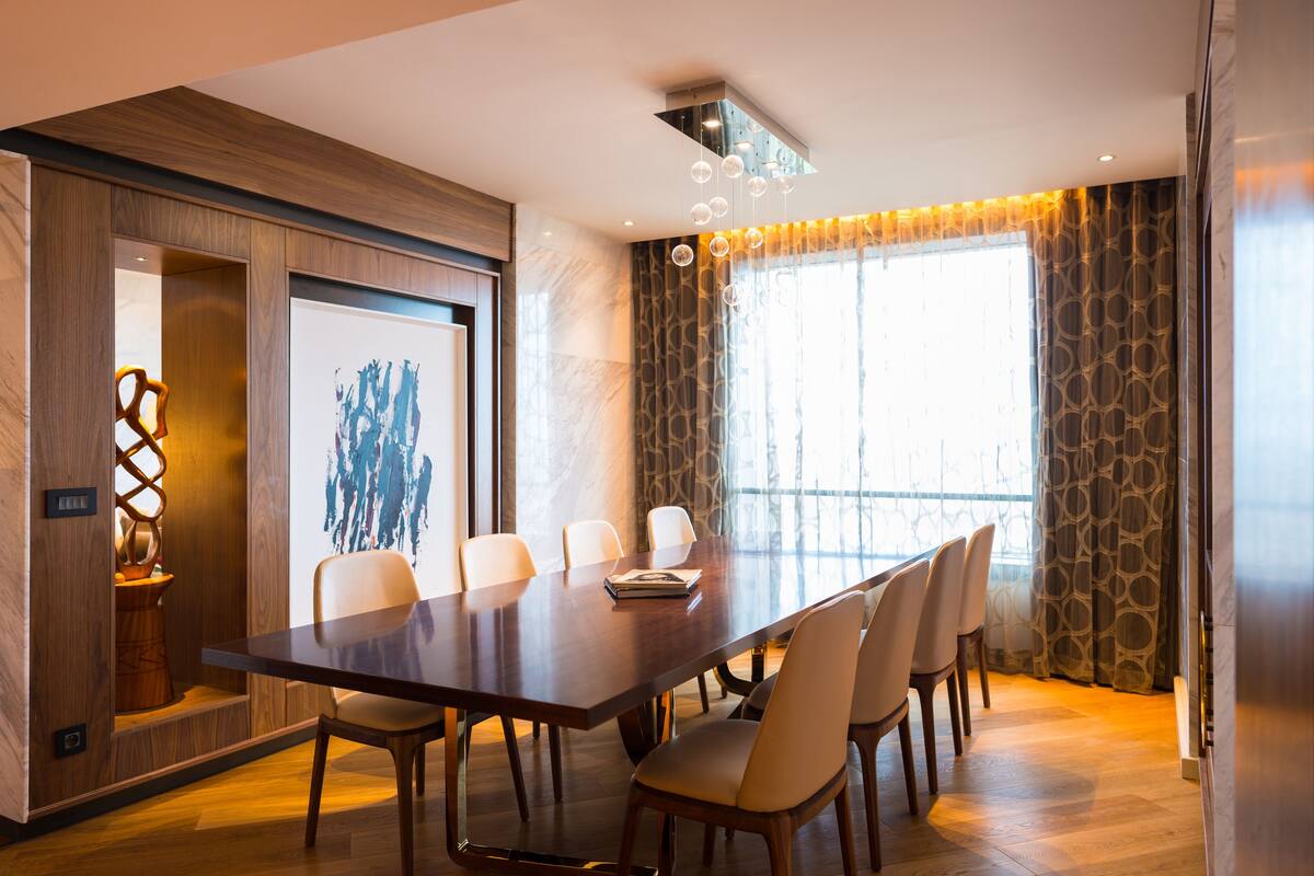Uma sala de conferências moderna com uma mesa comprida, seis cadeiras, um projetor e uma janela grande com cortinas estampadas.