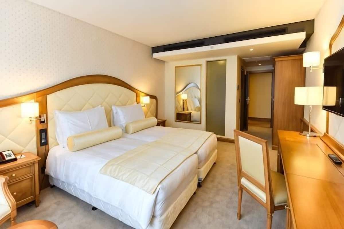 Quarto de hotel com uma cama grande, mesas de cabeceira, uma escrivaninha e um espelho.