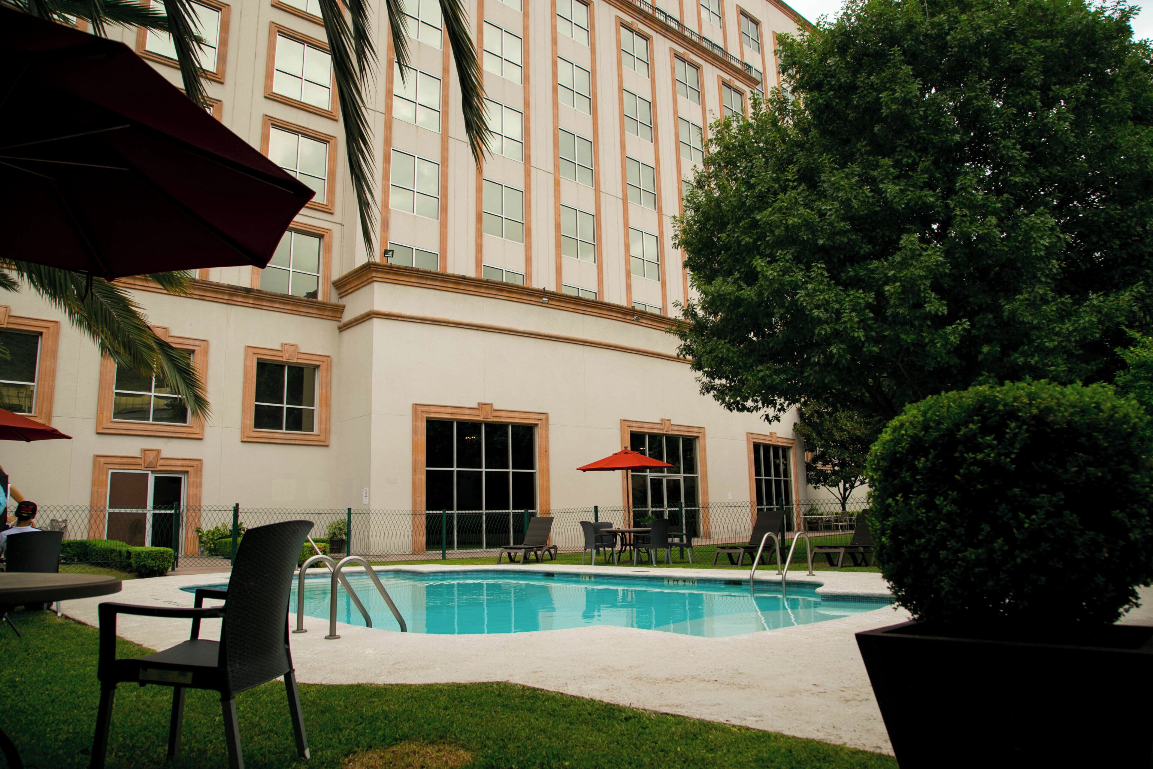 Pátio de hotel com piscina, área de estar ao ar livre e uma grande árvore.