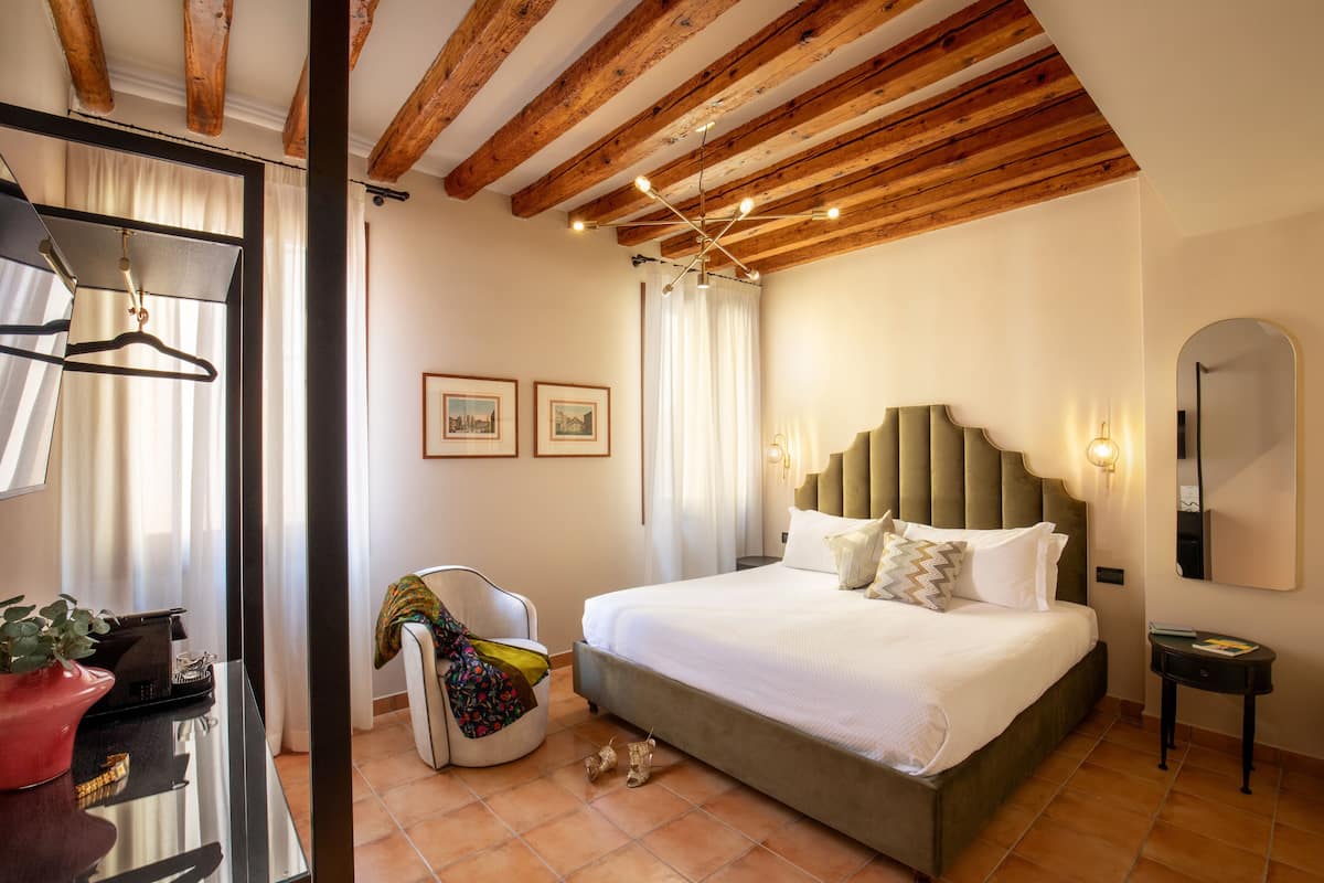 Um quarto com uma cama grande, vigas de madeira no teto, uma mesinha de cabeceira e um espelho.