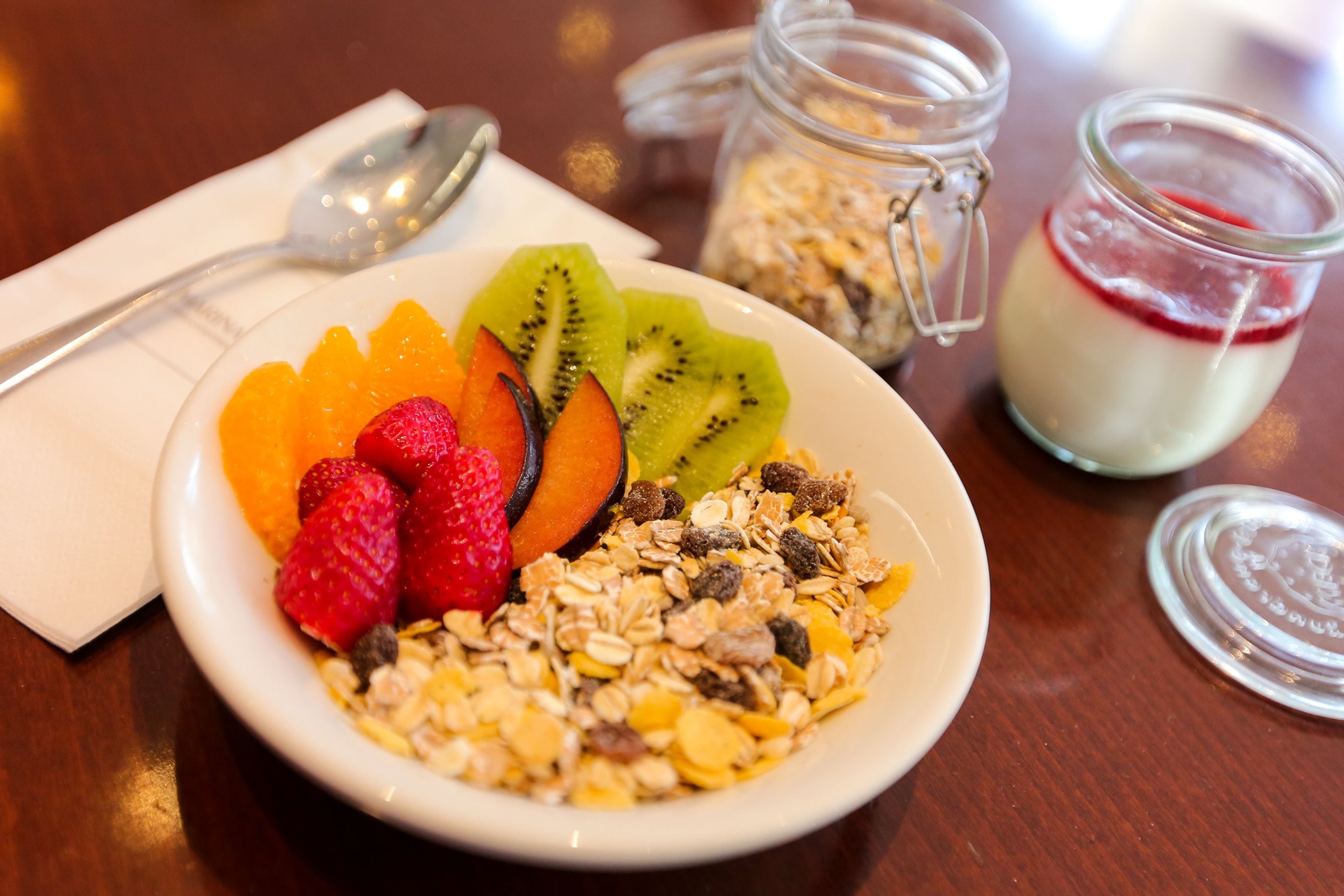 Uma tigela de cereais com frutas e uma colher sobre uma mesa.