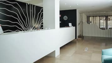 Uma área de recepção moderna com um balcão branco, uma parede preta com desenhos luminosos brancos e um relógio grande.
