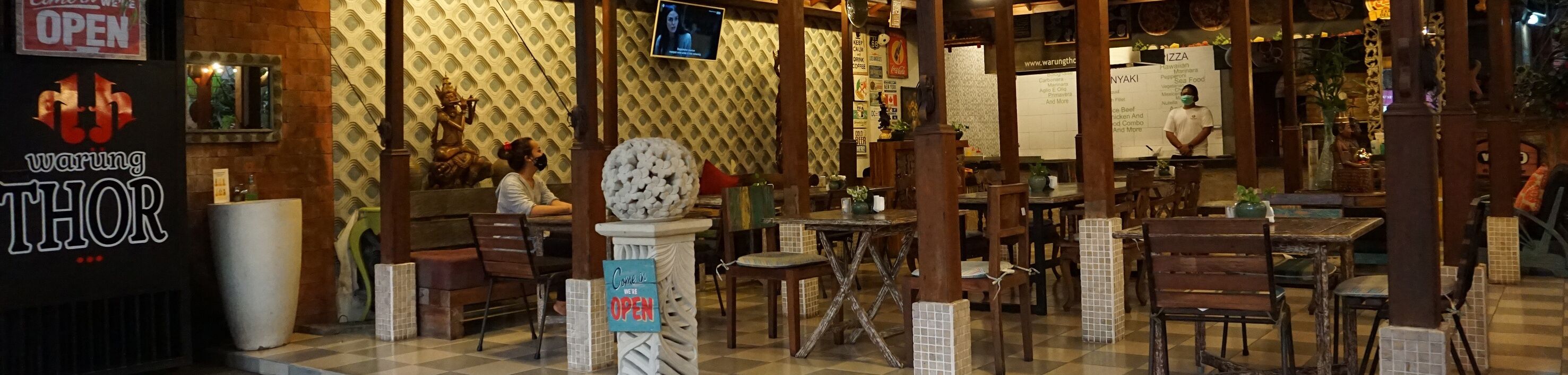 Interior de restaurante com chão xadrez, móveis de madeira e um letreiro indicando 'OPEN'.