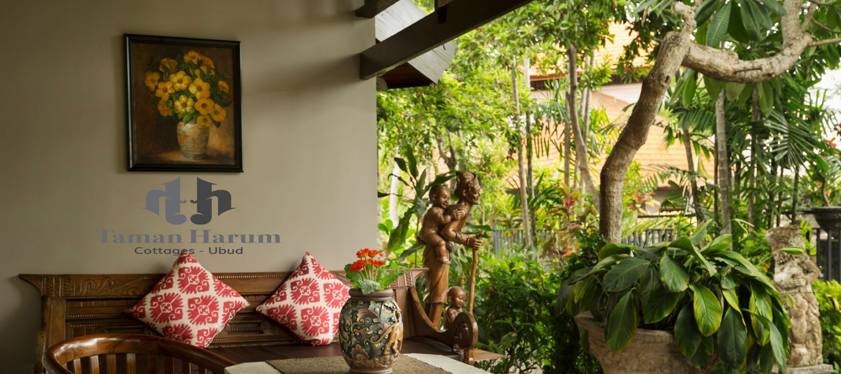 Um banco de madeira com almofadas estampadas, um vaso decorativo com flores e uma estátua em um jardim exuberante.