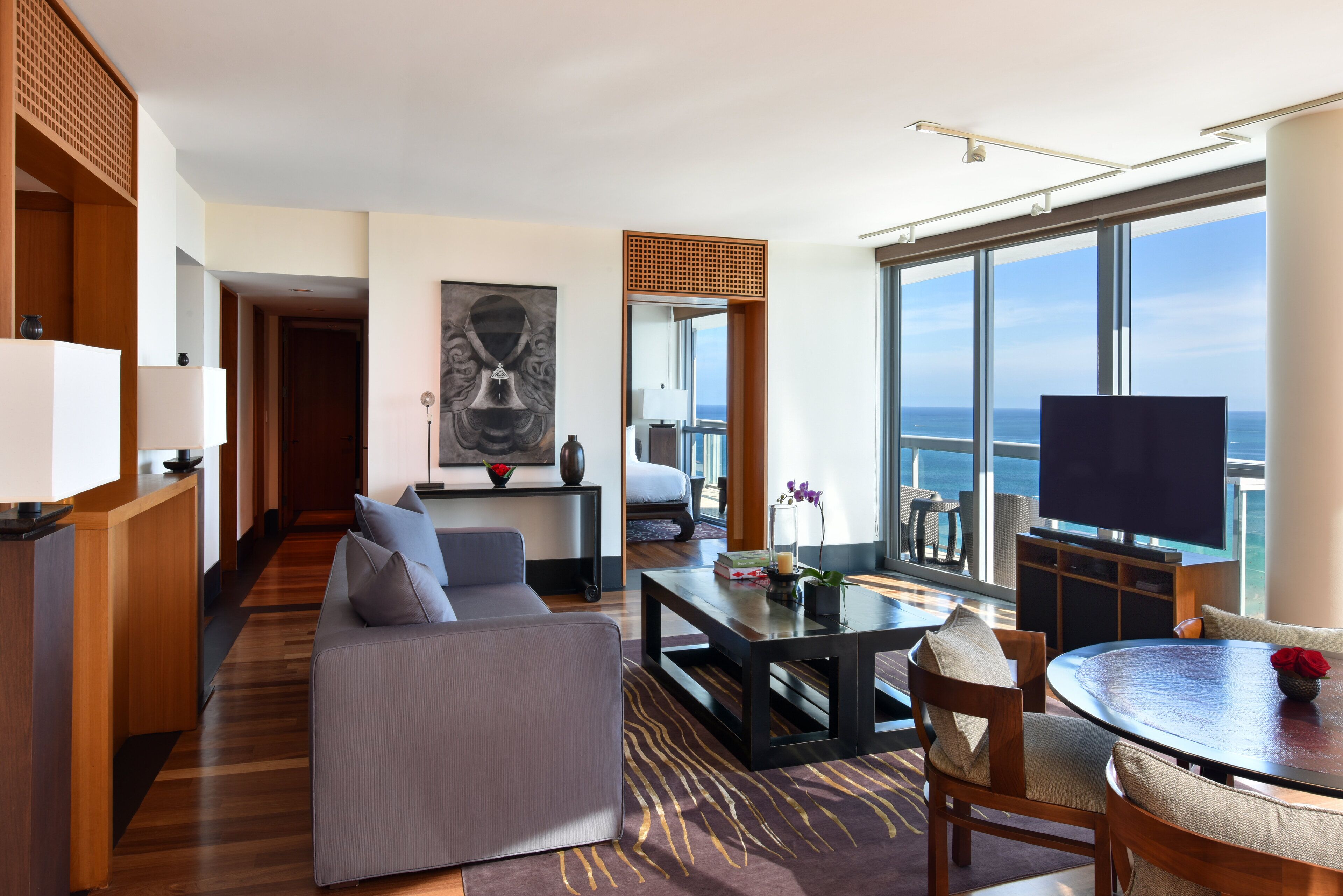 Quarto de hotel moderno com área de estar, mesa de jantar e uma televisão grande.
