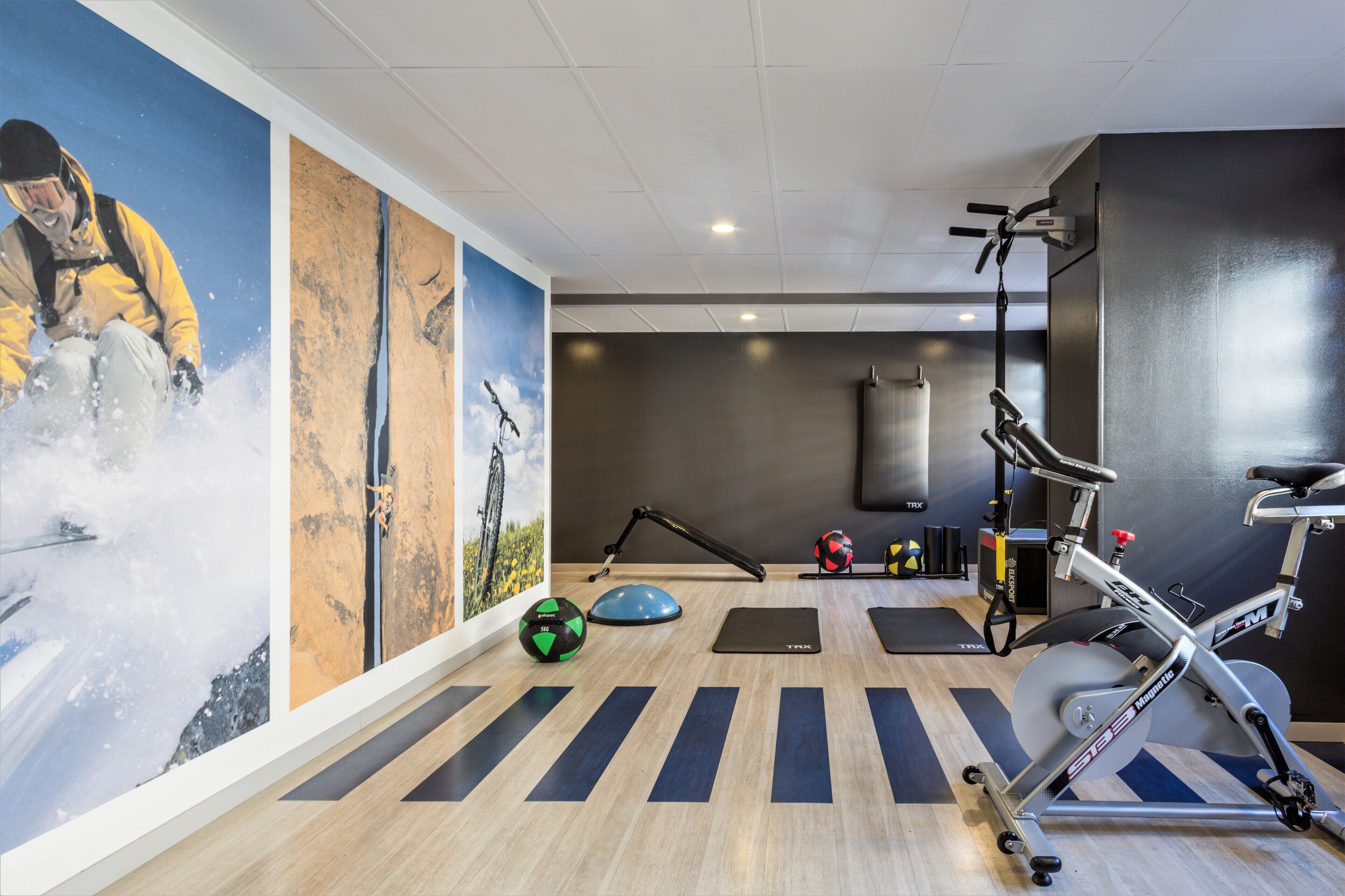 Uma academia com equipamentos de exercício, um mural e piso de madeira.