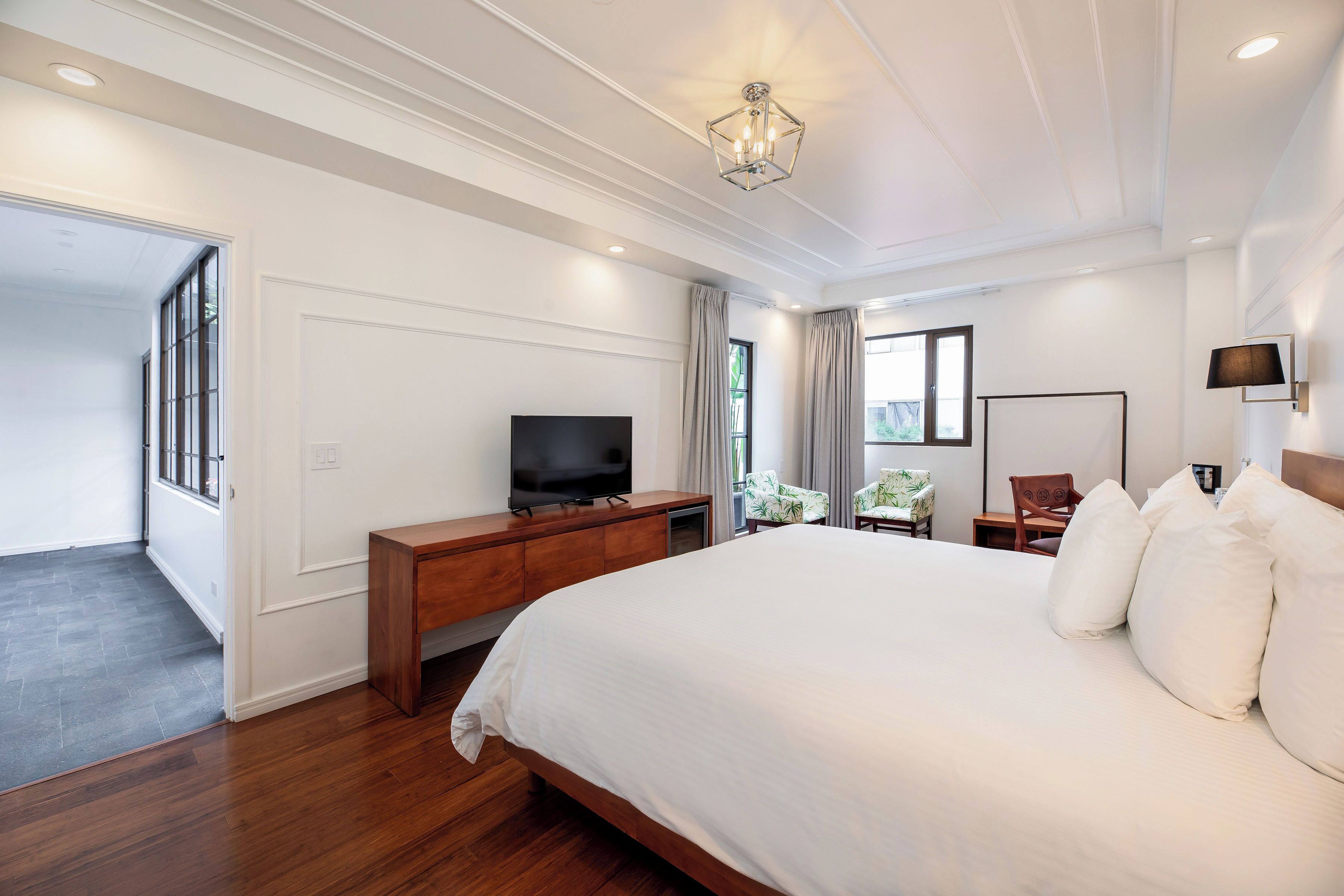 Quarto de hotel moderno com uma cama grande, cômoda de madeira, televisão de tela plana e escrivaninha com duas cadeiras.