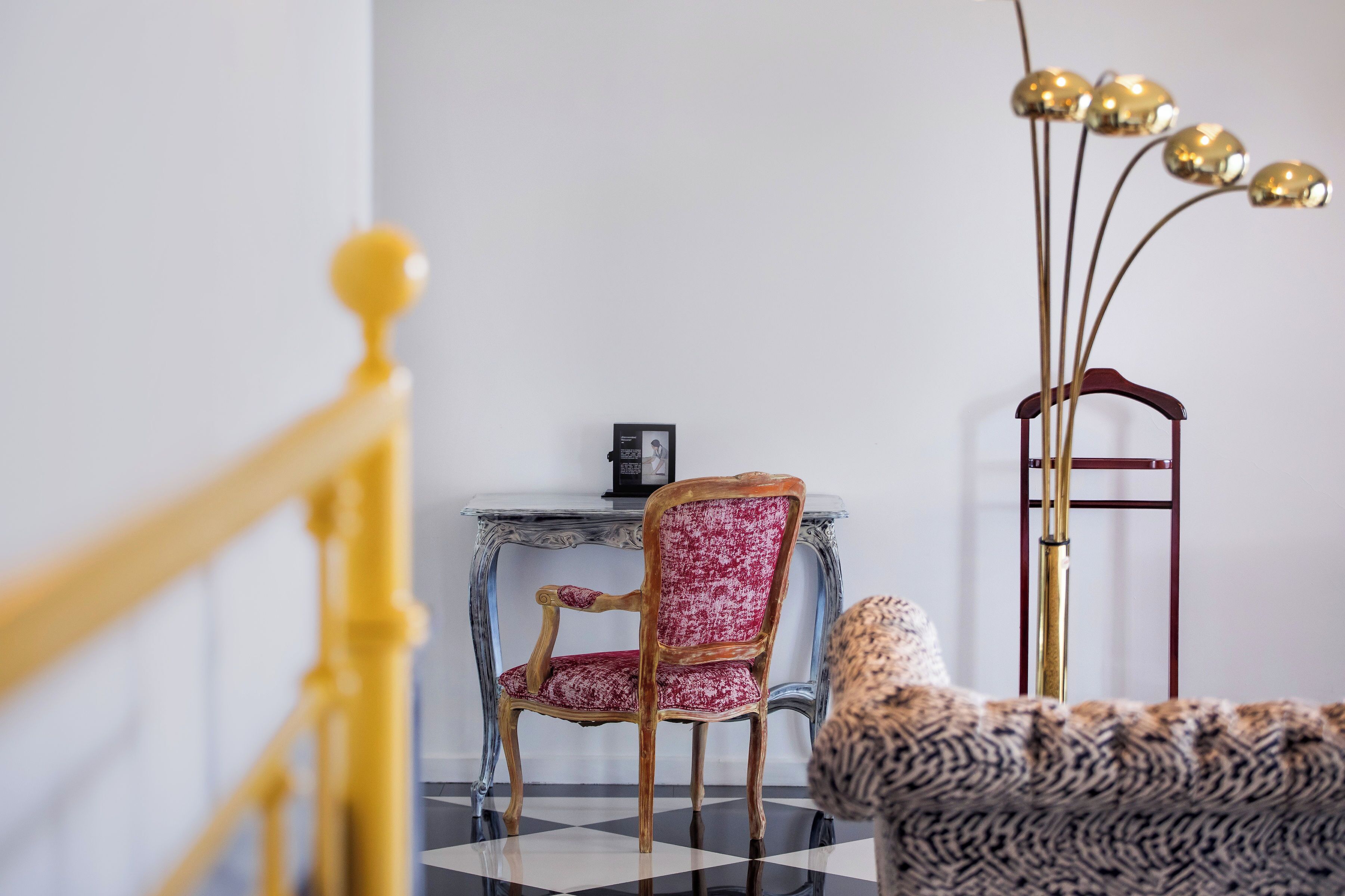 Um quarto com escada de madeira, uma poltrona vermelha estofada, uma escrivaninha de estilo vintage e um abajur com design exclusivo.